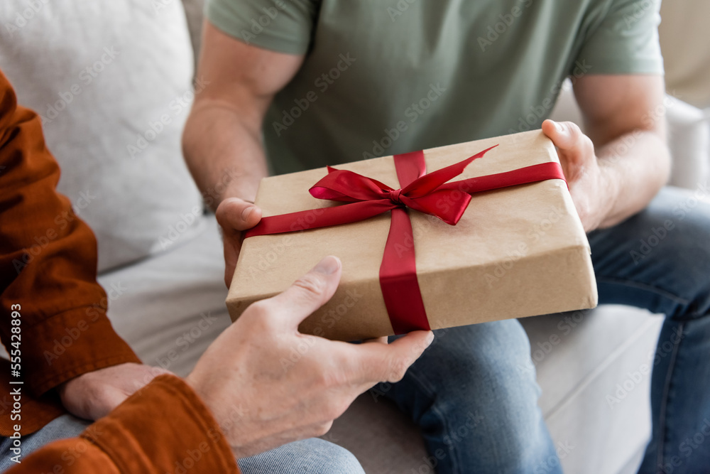 partial view of man holding gift box with red ribbon while ...
