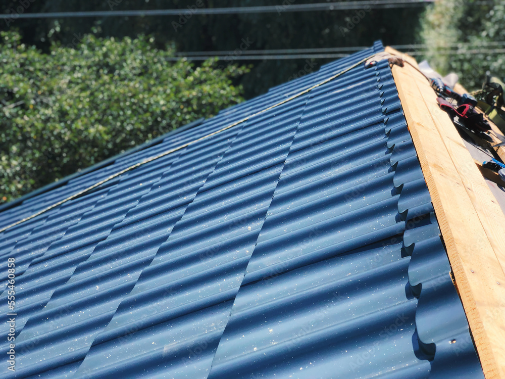 Laying metal tiles on the corner of the roof during the day under the ...