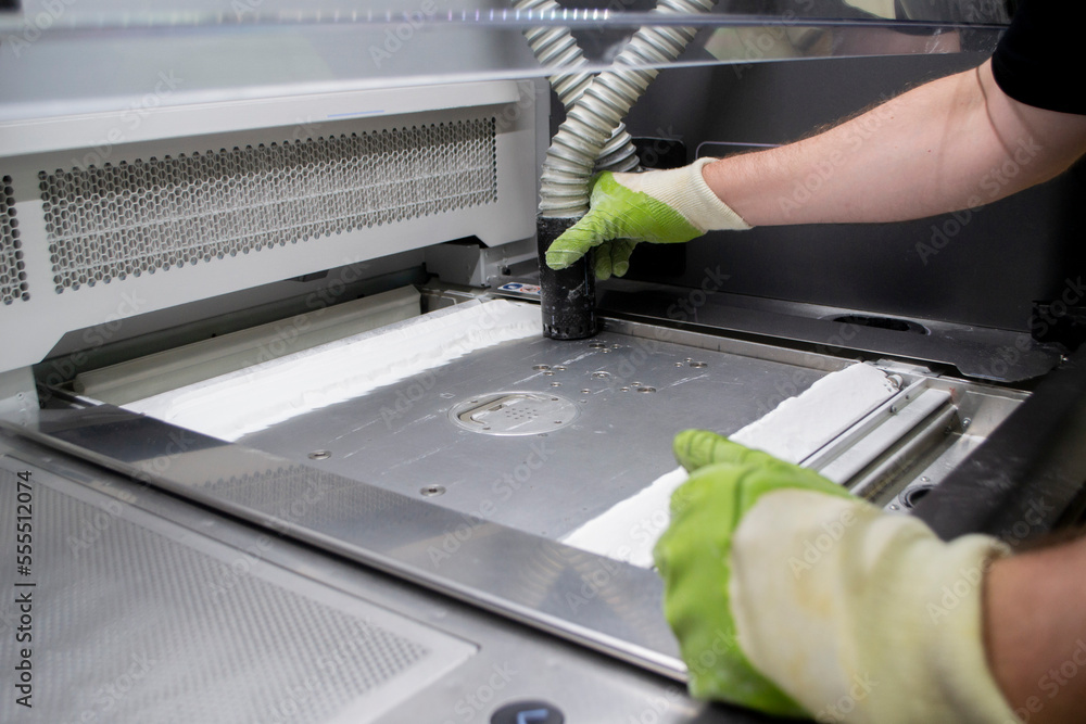 A male worker cleans the surface of an industrial 3D printer from white ...