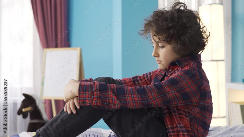 Sad child is sitting on the bed in the room. Frustrated unhappy child ...