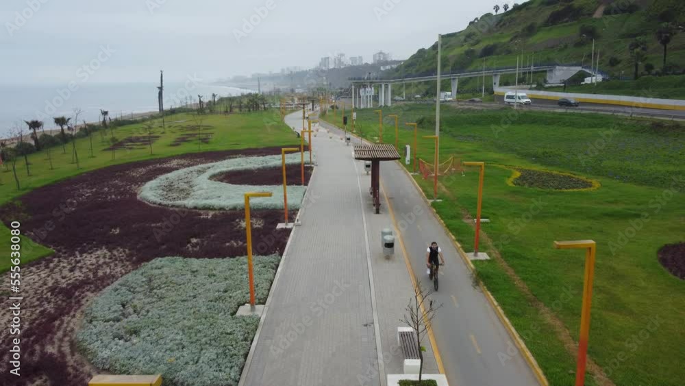 Drone slowly flies forward above coastal park walkway. People on ...