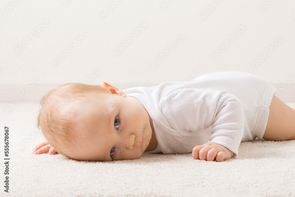 Tired adorable baby boy in white bodysuit lying down on belly and ...