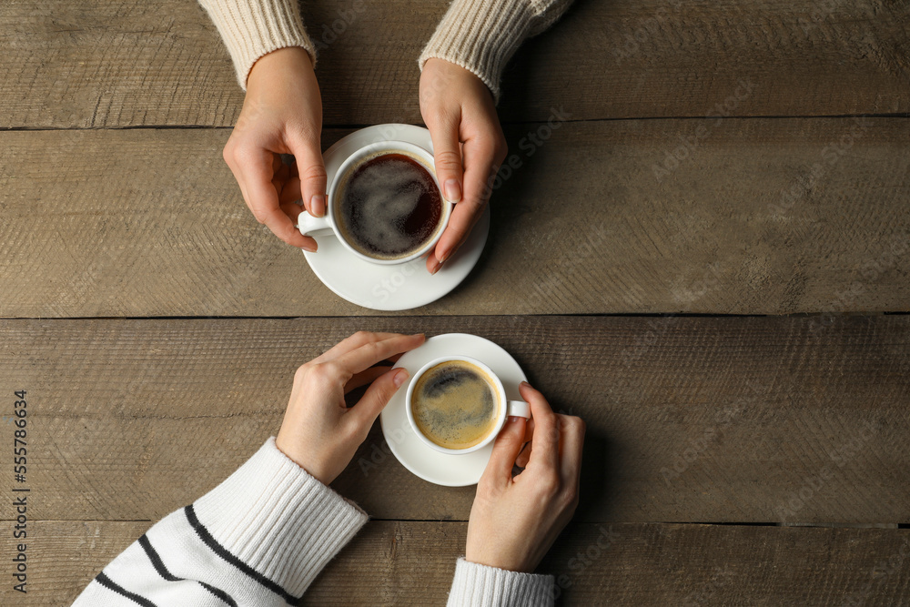Women with cups of aromatic coffee at wooden table, top view. Space for ...