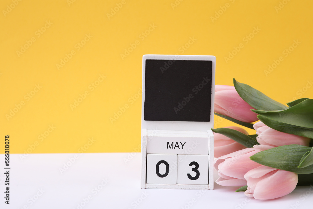 Block wooden calendar with the date may 03 and tulips on a pastel ...