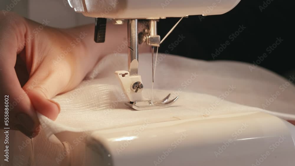 Close-up shot of sewing machine sews a line, a seamstress woman cuts ...