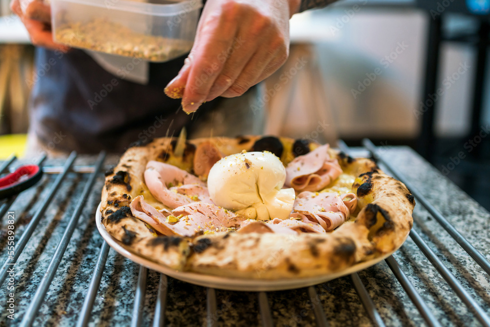 Neapolitan pizza style: close-up chef hand seasoning crushed pistachio ...
