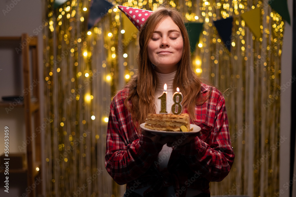 Happy 18 years old girl in party cone make a wish and blowing out ...