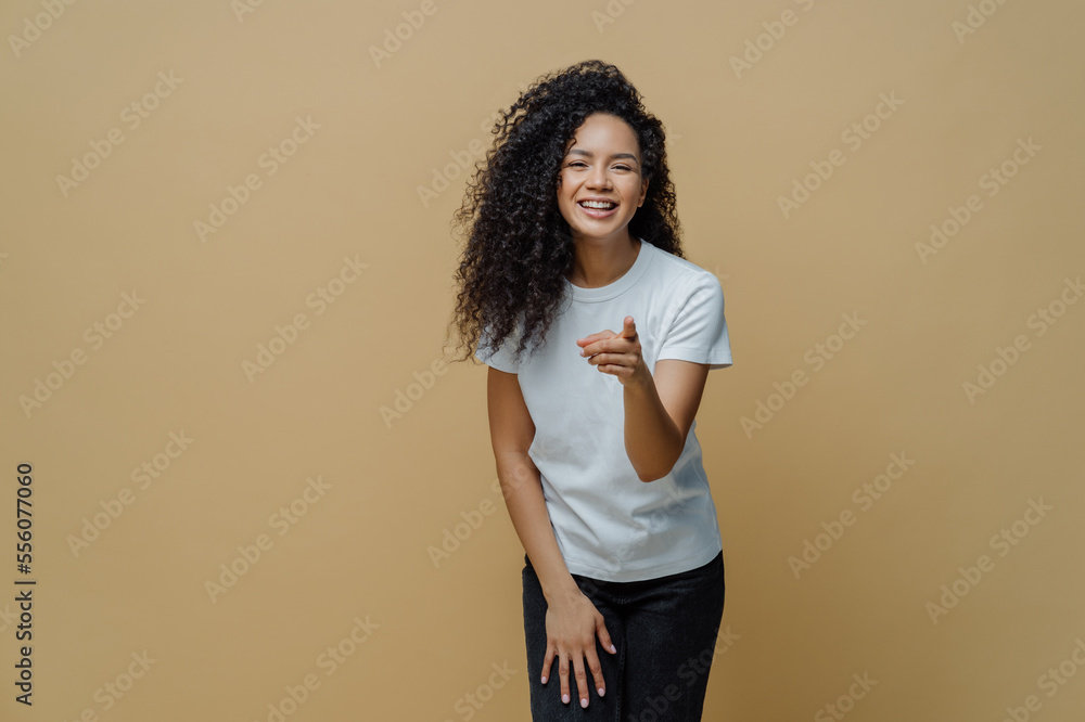 Cheerful energetic young woman with curly Afro hair points index finger ...