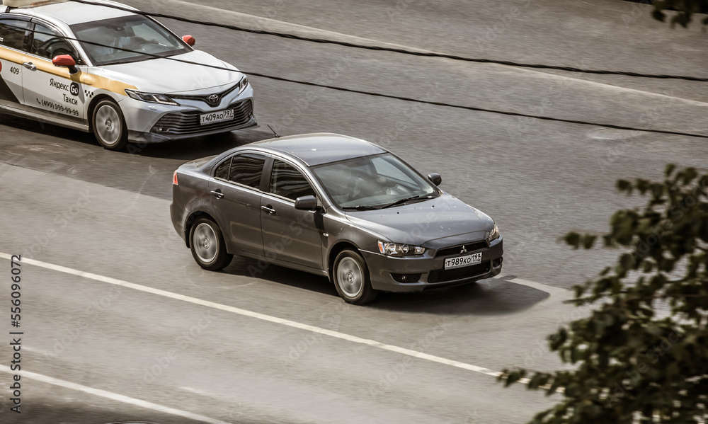 Mitsubishi Lancer at the city road in motion. Gray car driving along ...