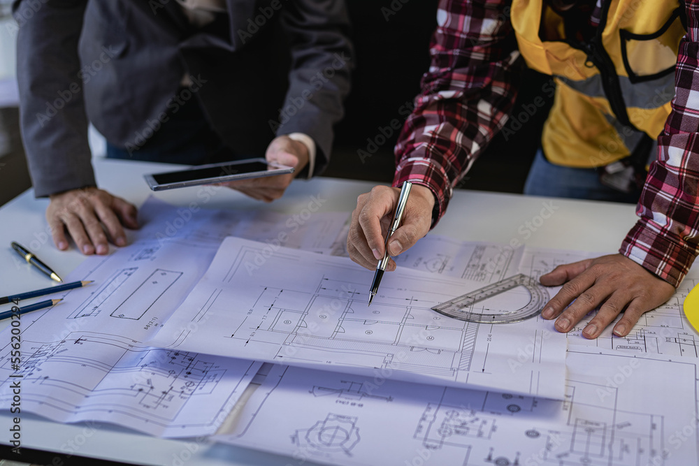 Engineer pointing at blueprint and using laptop to draw building design ...