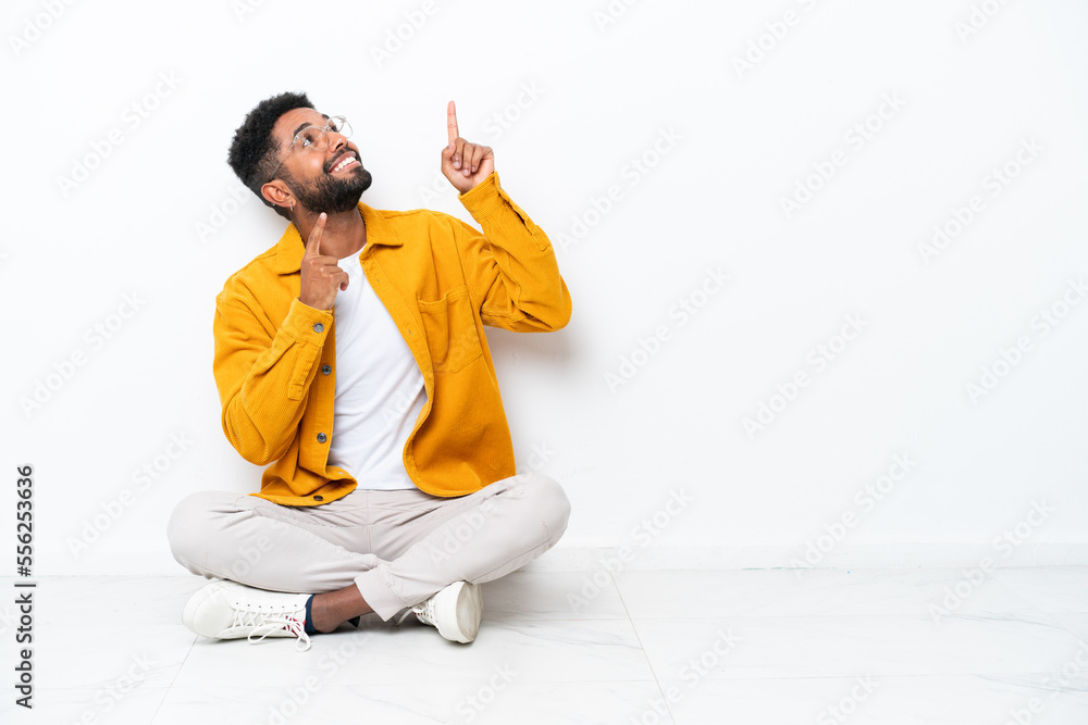 Young Brazilian man sitting on the floor isolated on white background ...