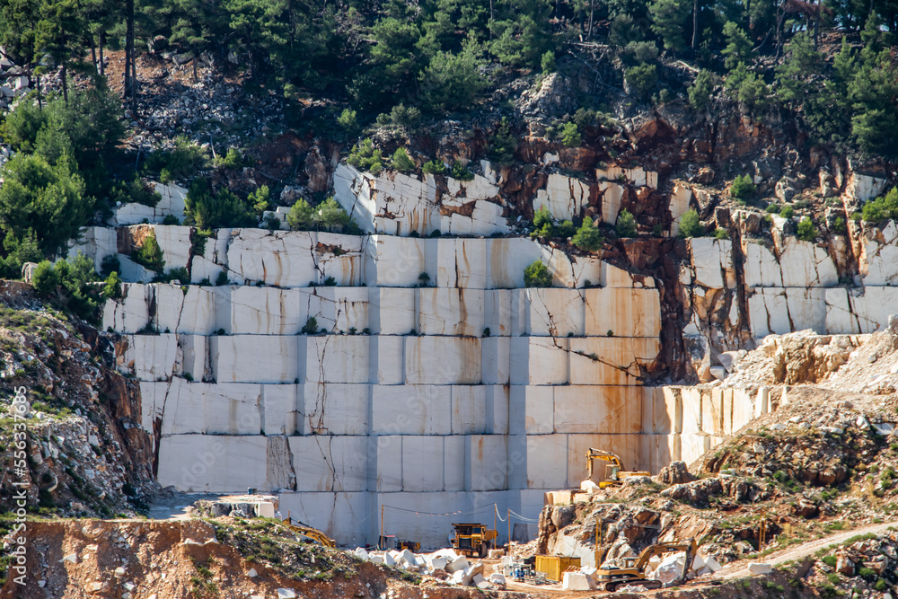 An open-pit mine of white marble stone with heavy machinery used to ...