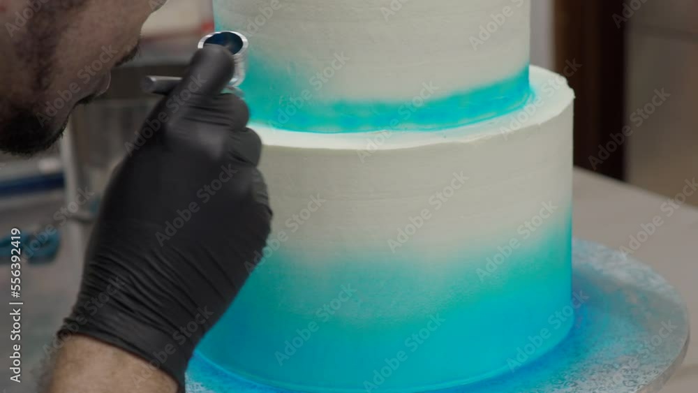 professional baker using edible airbrush colours to decorate two floor ...