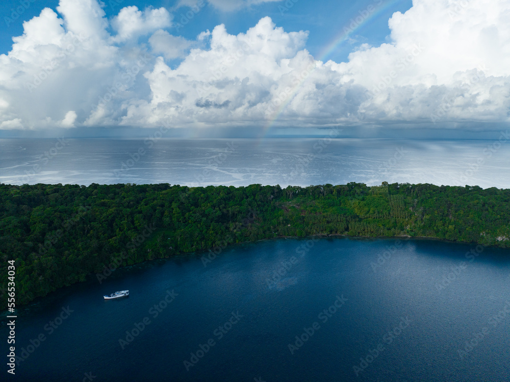 A faint rainbow appears behind a remote tropical island in the Solomon ...