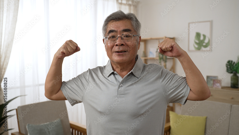 Strong elderly gray-haired man wearing glasses standing showing biceps ...