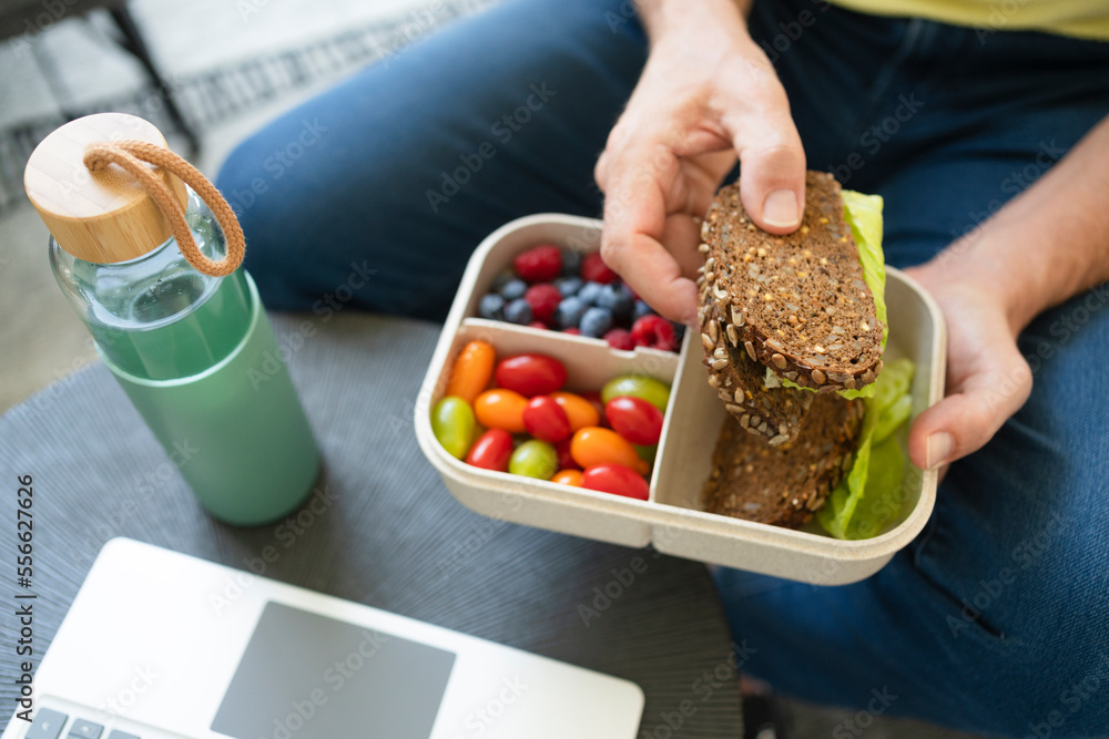 Hand of man holding sandwich above lunch box Stock Photo | Adobe Stock