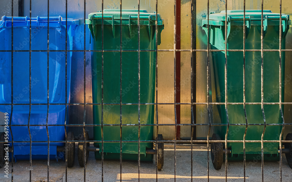 Garbage multi-colored outdoor plastic bins behind a metal grate ...