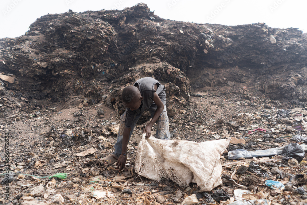 African slum boy collecting reusable items in a garbage dump; symbol of ...