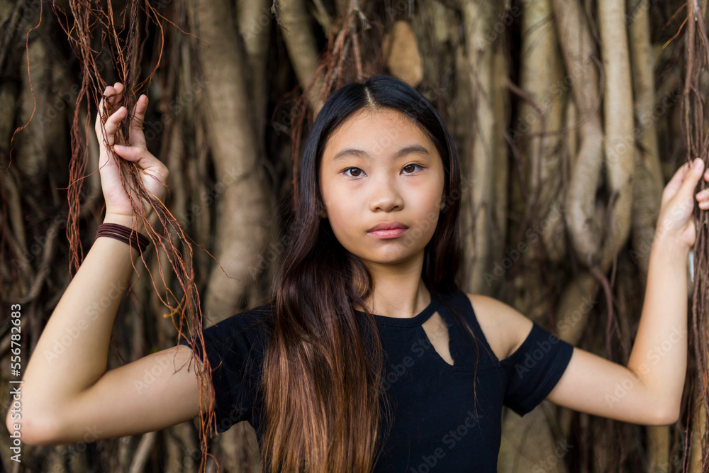 Portrait of a preteen girl standing among vines and tree roots; Hong ...
