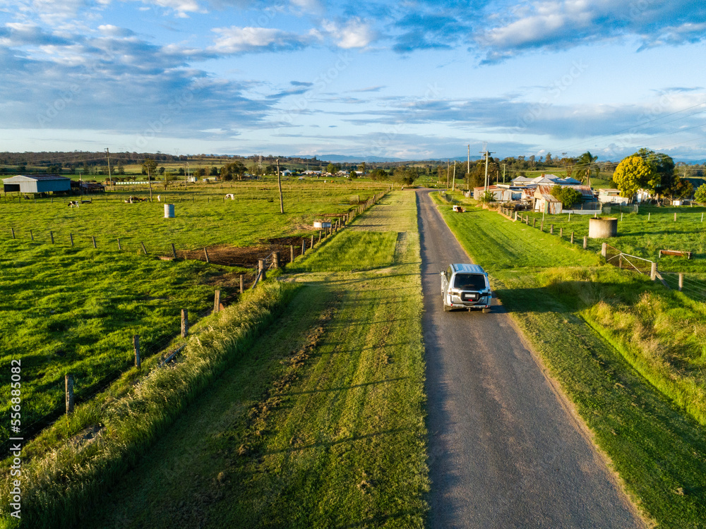 Four wheel drive car travelling through farmland on narrow country road ...