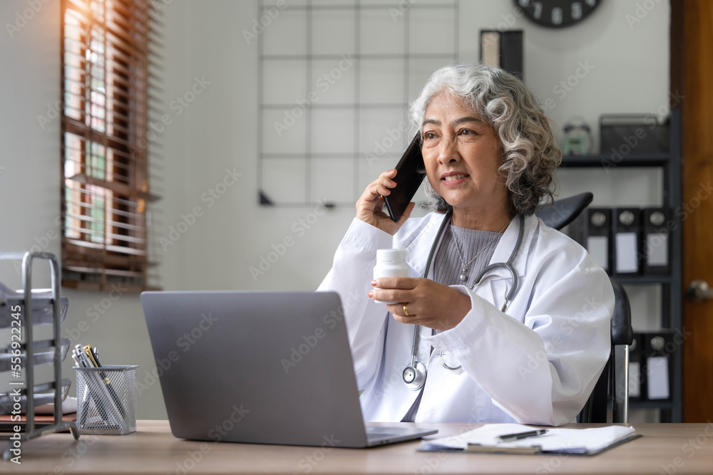 Senior asian female doctor using mobile phone talking while sitting in ...