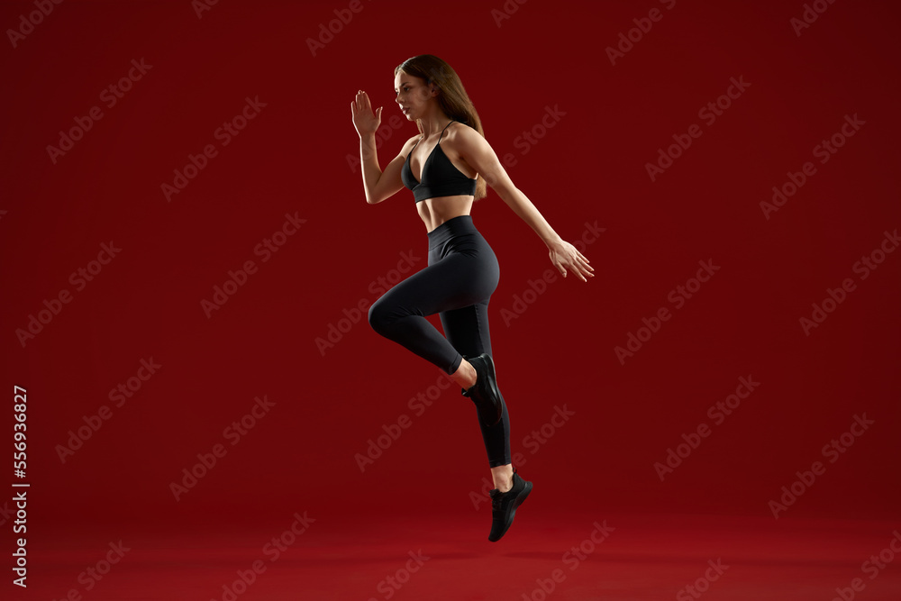 Side view of brunette athletics woman jumping on one leg highly in red ...