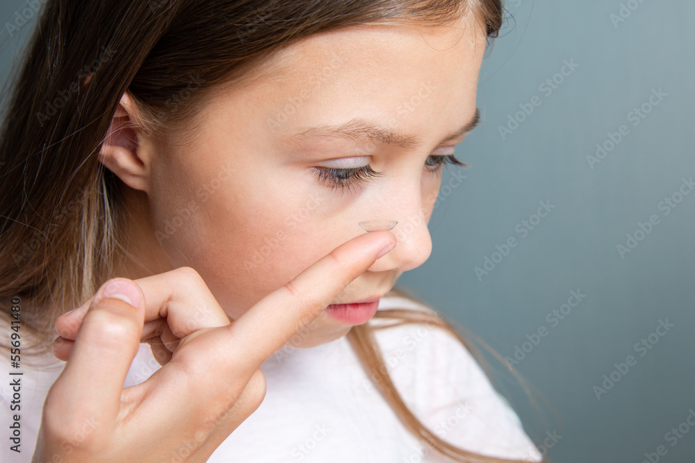 Little child girl inserting a transparent contact lens into her eye on ...