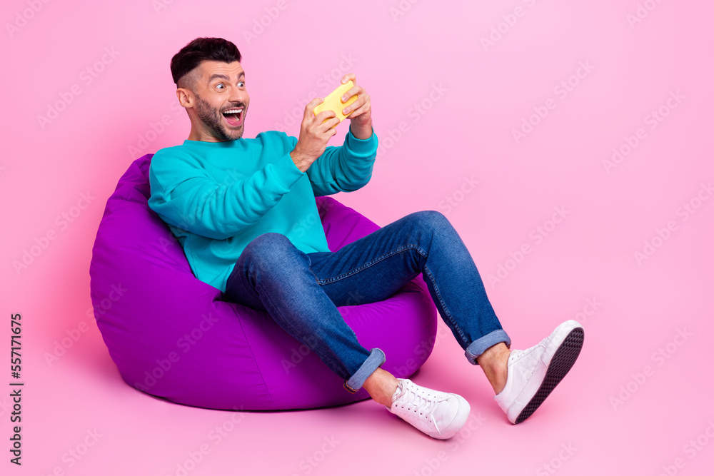 Full size photo of young handsome male sit bean bag play mobile game ...