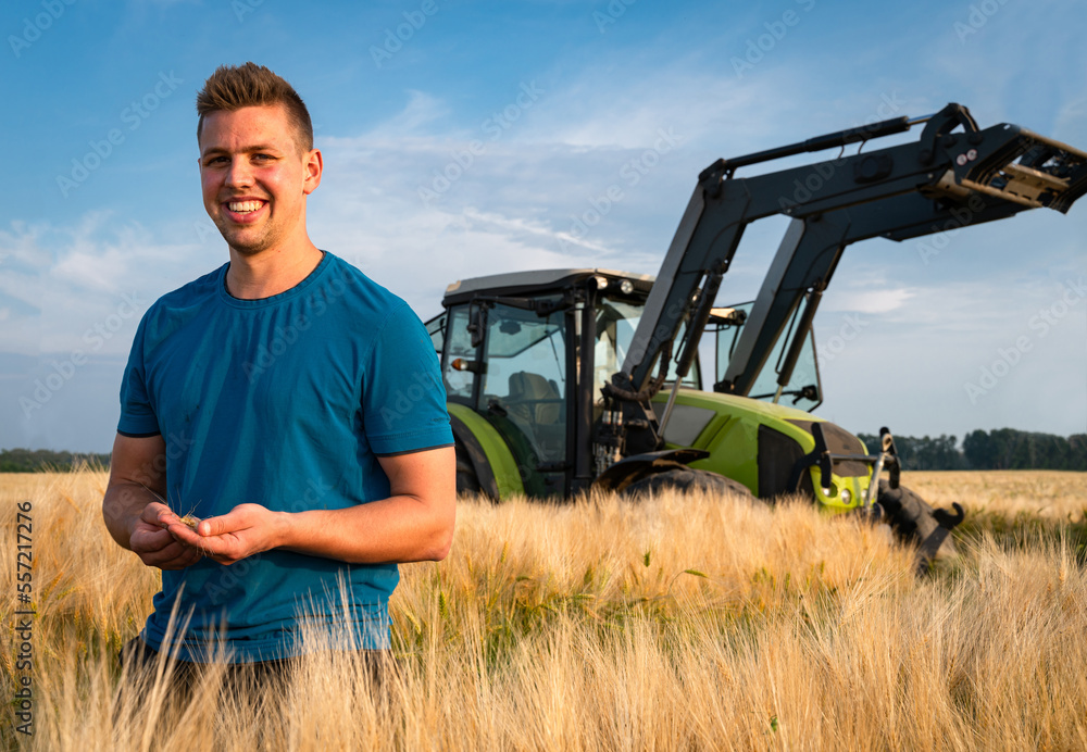 Junger Landwirt steht mit seinem Traktor an einem reifen Getreidefeld ...