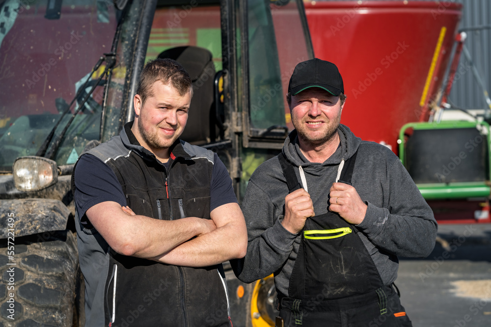 Landwirt mit seinem Sohn bei der Arbeit auf dem Hof, stehen am Hoftrac ...
