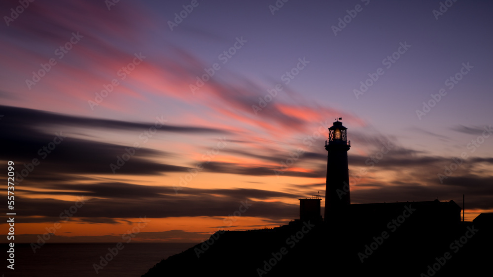 Lighthouse at sunrise with coloured sky and sea creating silhouette ...