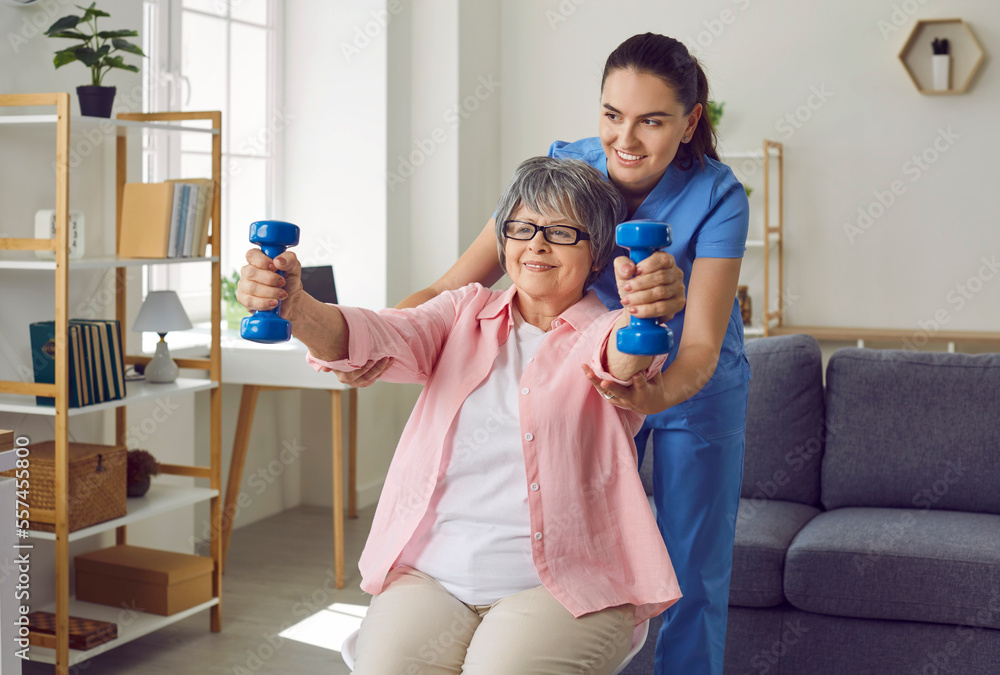 Smiling senior woman lifting dumbbells, therapist assisting her ...