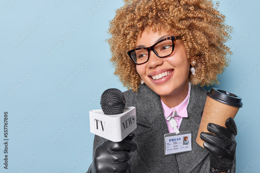 Horizontal shot of curly haired professional female TV presenter holds ...