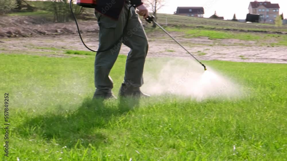 Farmer spraying pesticide on lawn field wearing protective clothing ...