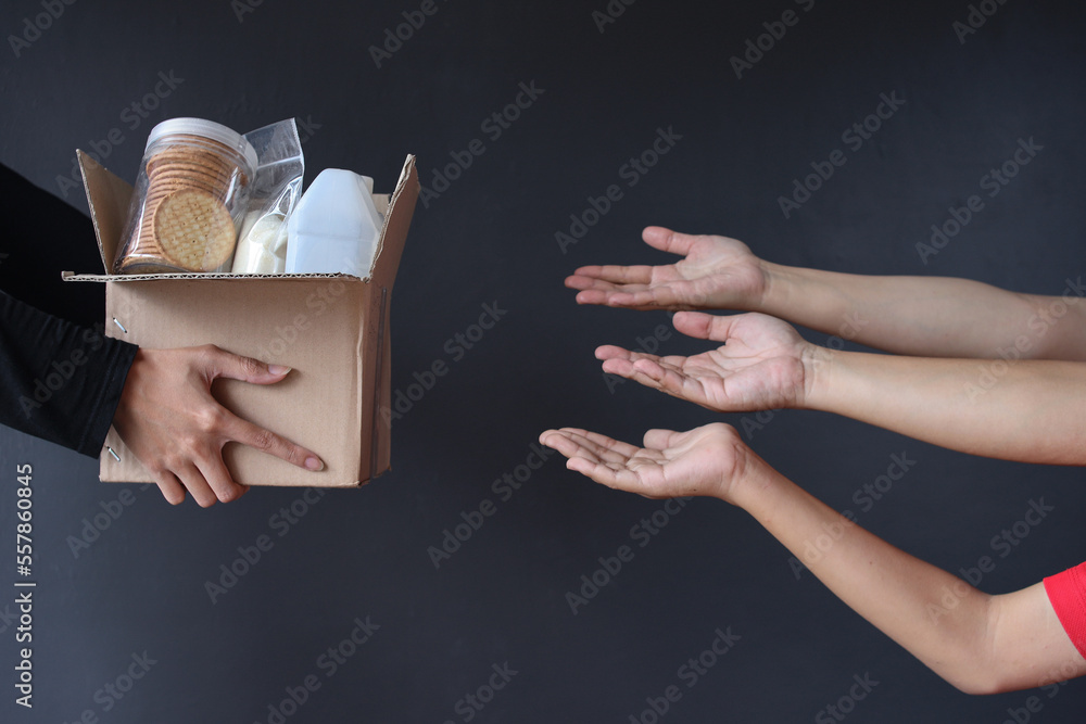 Hand giving box of various foods to many hands on dark gray background ...