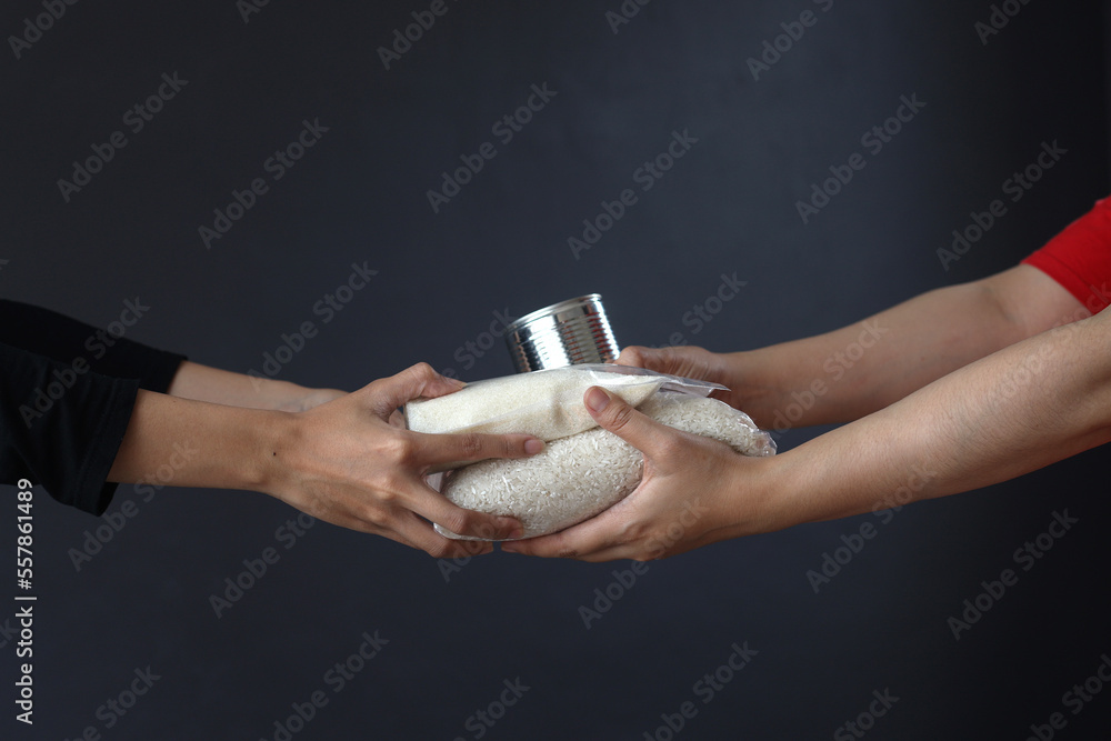 Hands giving and receiving staple food for donation and charity on dark ...