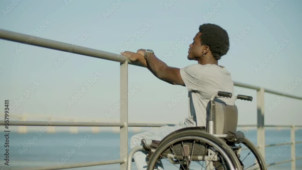 Young Black man in wheelchair enjoying sea view. Side view of happy guy ...