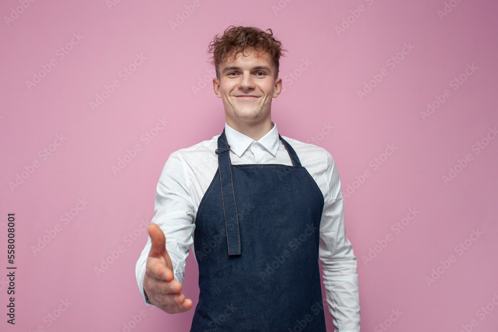 young waiter in a white shirt and an apron extends his hand and greets ...