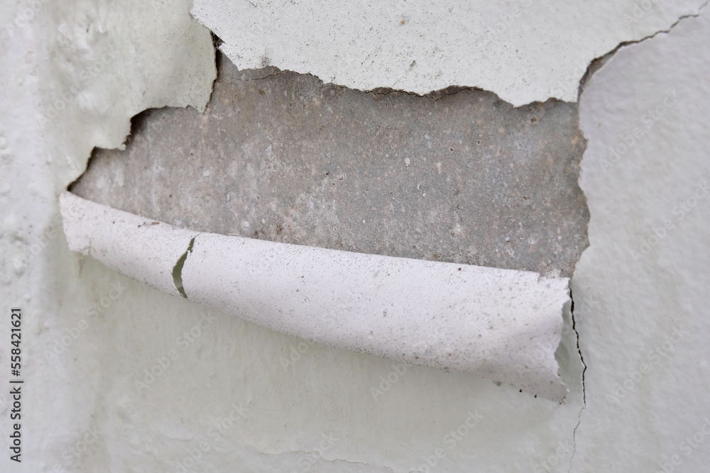 A layer of white paint peeling from a concrete wall due to effects of ...