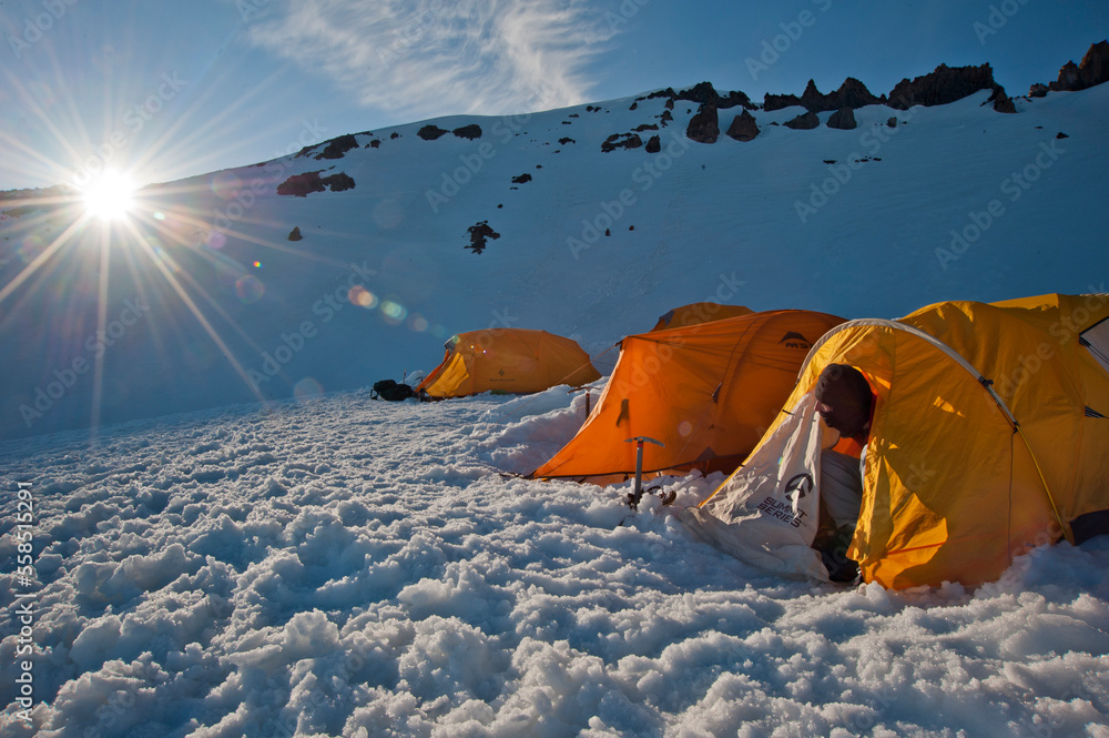 A climber watches the sun set over a ridge from a camp on Mount Shasta ...