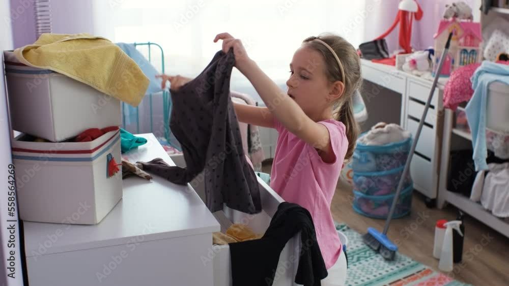 Little girl folding clothes and putting it in the drawers, doing room ...