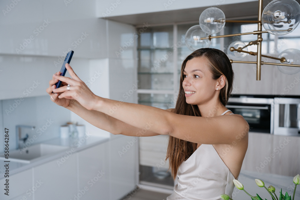 Foto de Adorable caucasian woman in nightie makes selfie at kitchen ...