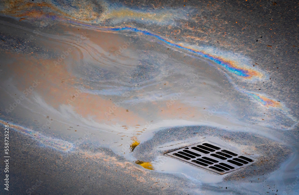 Oil slick on the asphalt road background drains into the storm drain ...