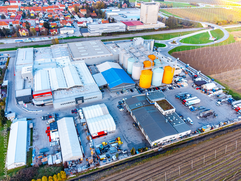Aerial view of a factory lot with warehouses and silos and town skyline ...