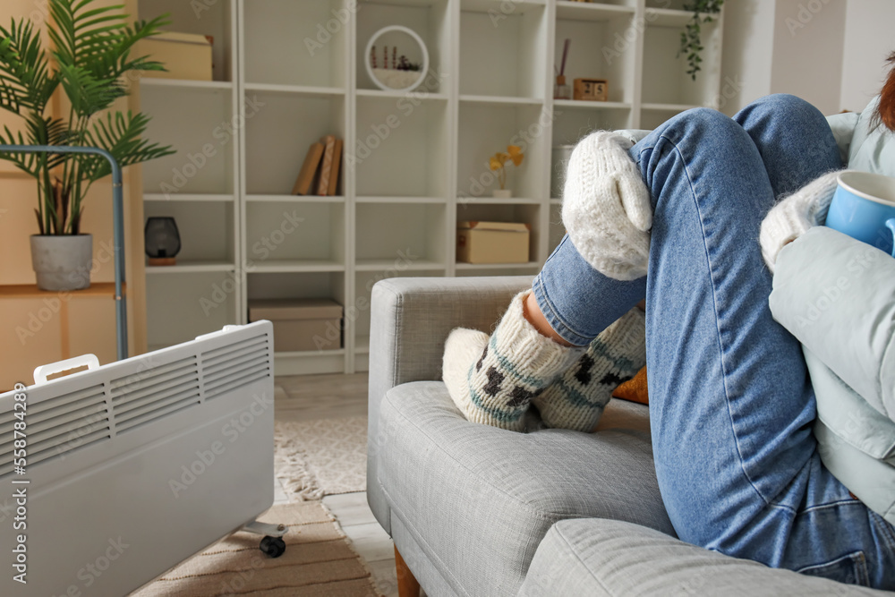 Frozen young woman in winter clothes with cup of tea warming near ...