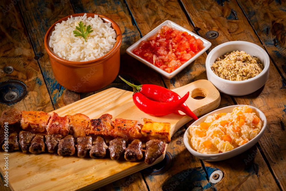 Espetinhos de churrasco em tábua de madeira com acompanhamentos, arroz ...