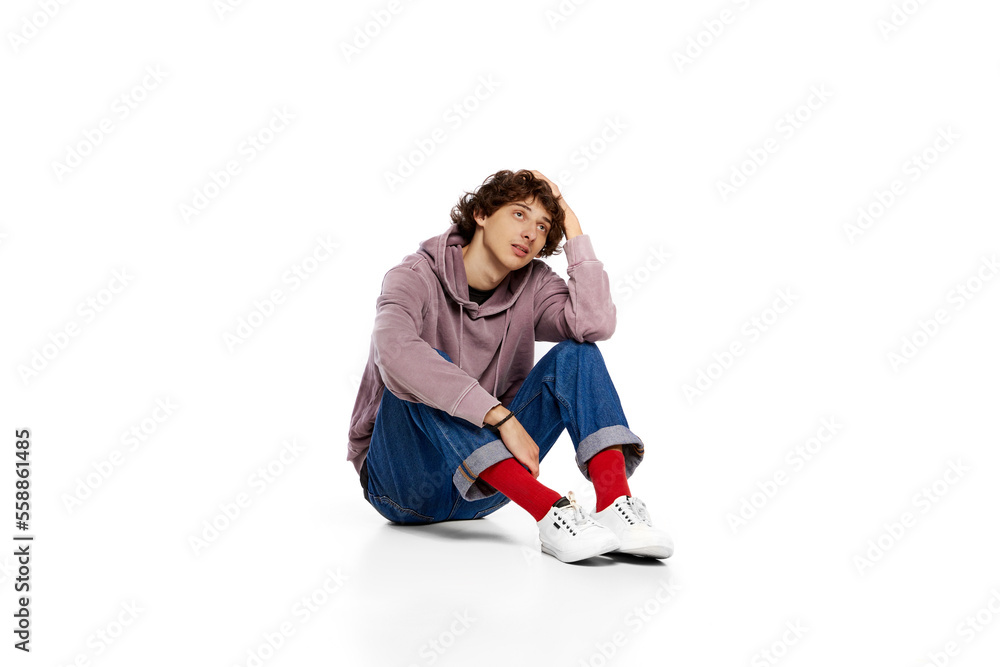 Portrait of young boy sitting over white background. Feeling sad ...