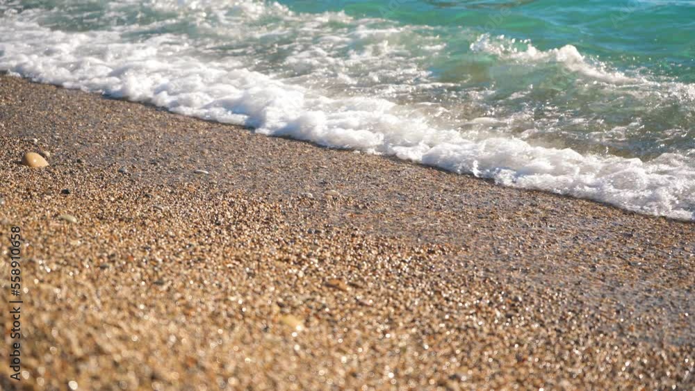 Rough sand beach, lit by sun, sea water washes over, closeup detail ...