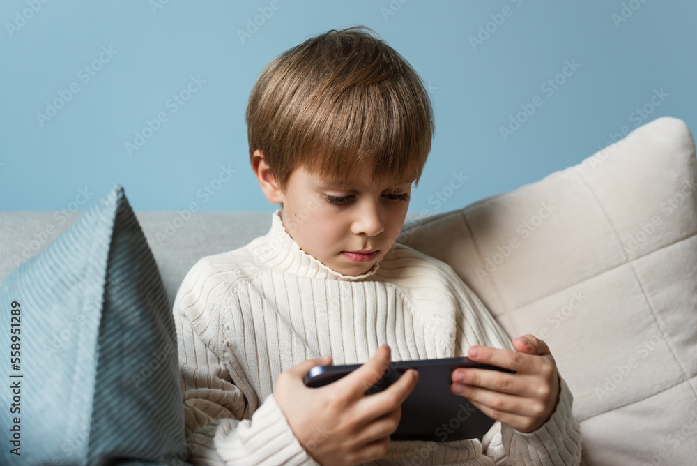 Boy spends time behind a screen on a tablet on the sofa in the living ...