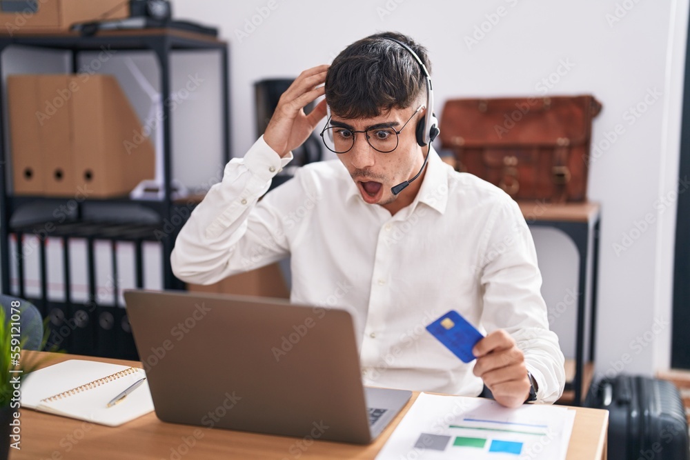 Young hispanic man working using computer laptop holding credit card ...